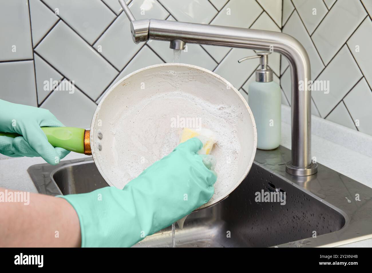 Hands in gloves scrub a spoon with a sponge under running water ...