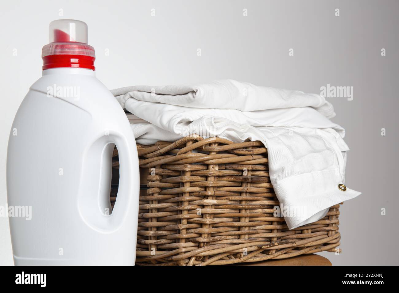 Laundry basket filled with stack of folded white clothes, detergent ...