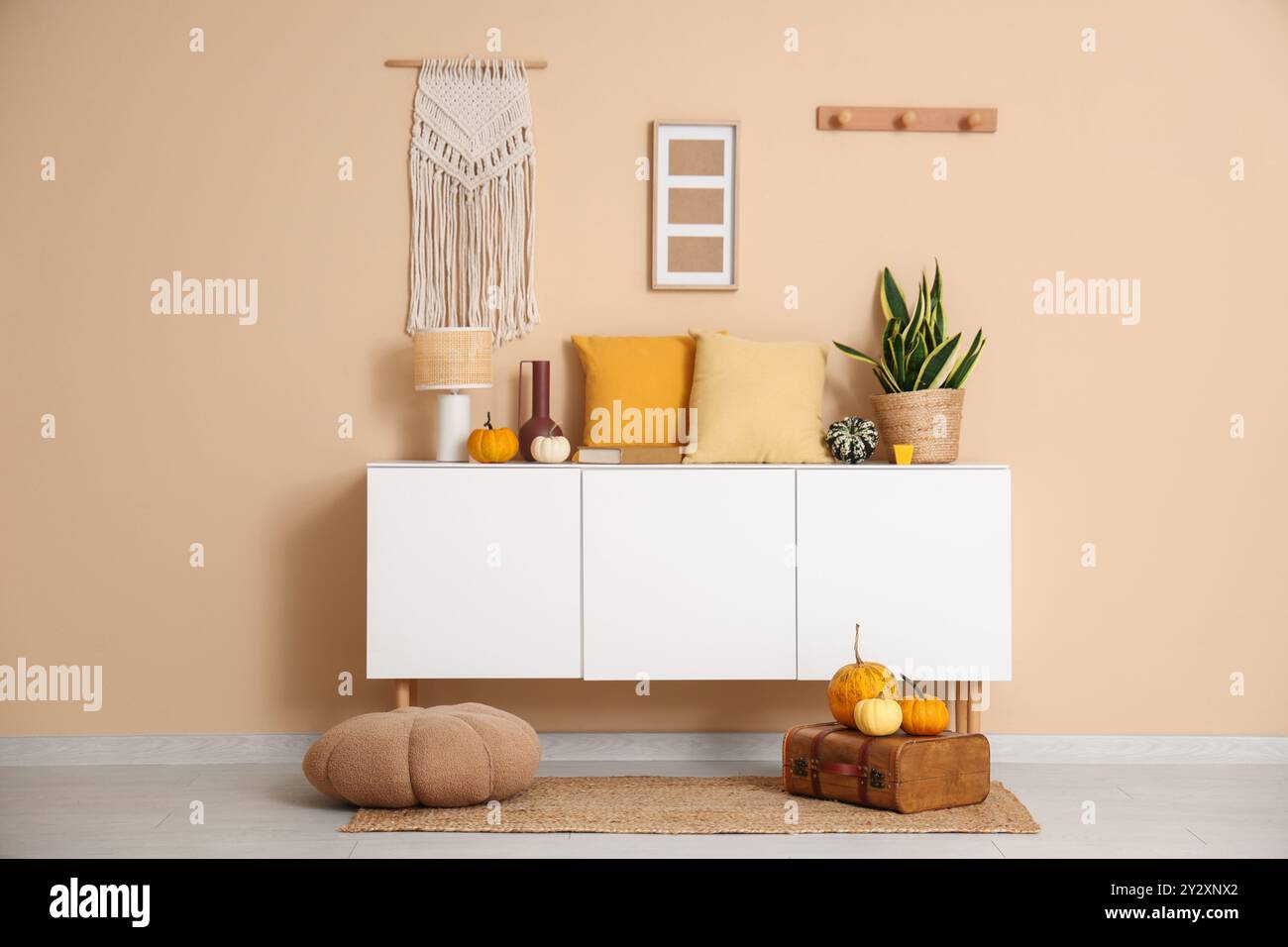 Modern chest of drawers, suitcase with pumpkins and pouf near beige ...