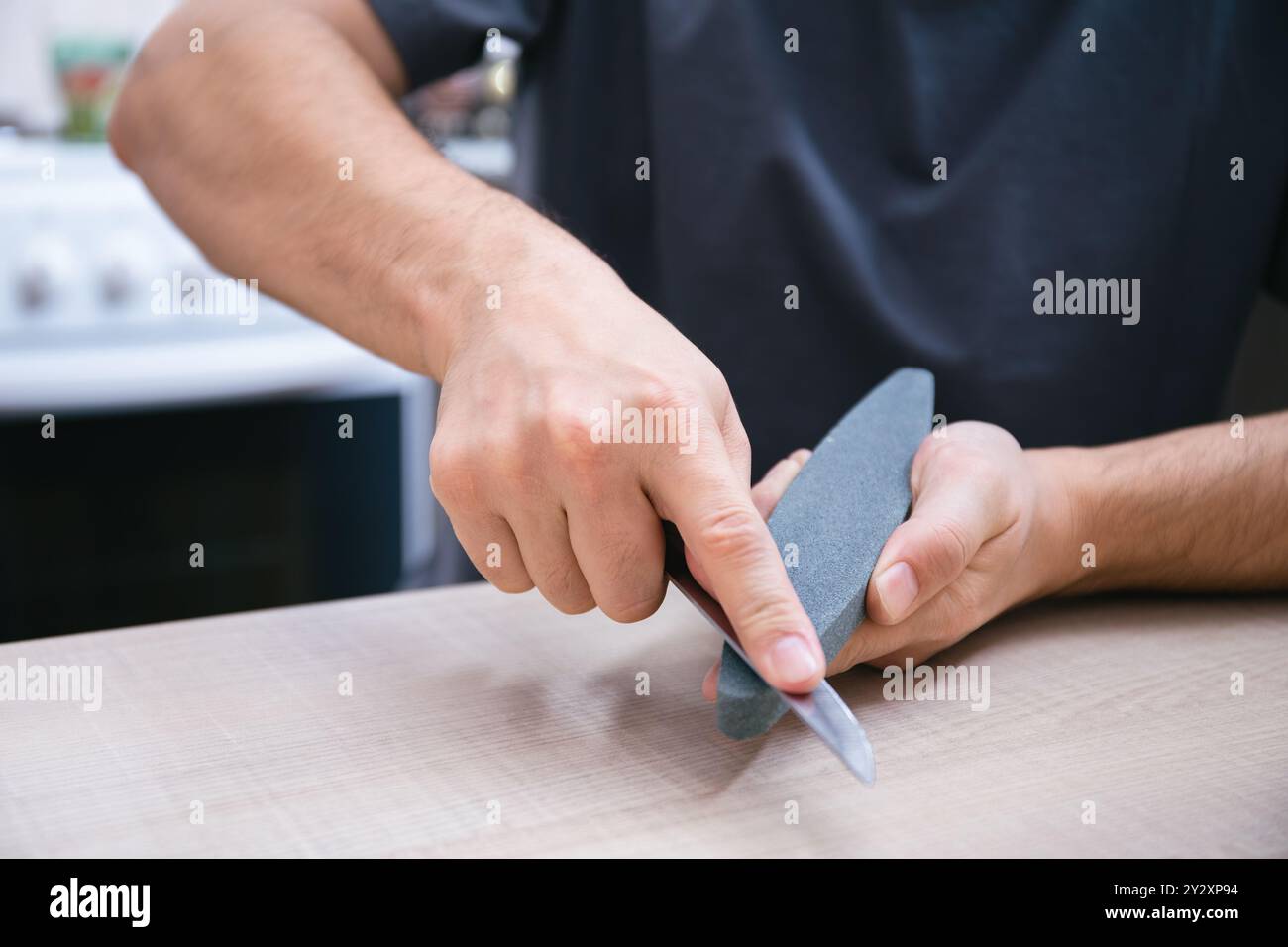 Hands sharpen a metal knife blade on sharpening stone,making the blade ...