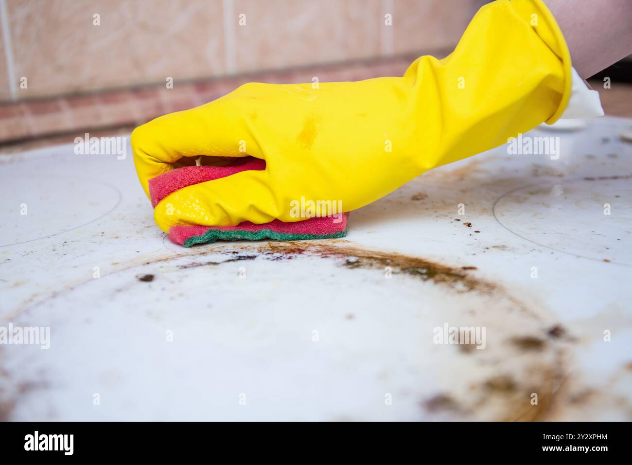 Hand in yellow gloves scrubbing dirty stovetop with sponge and ...