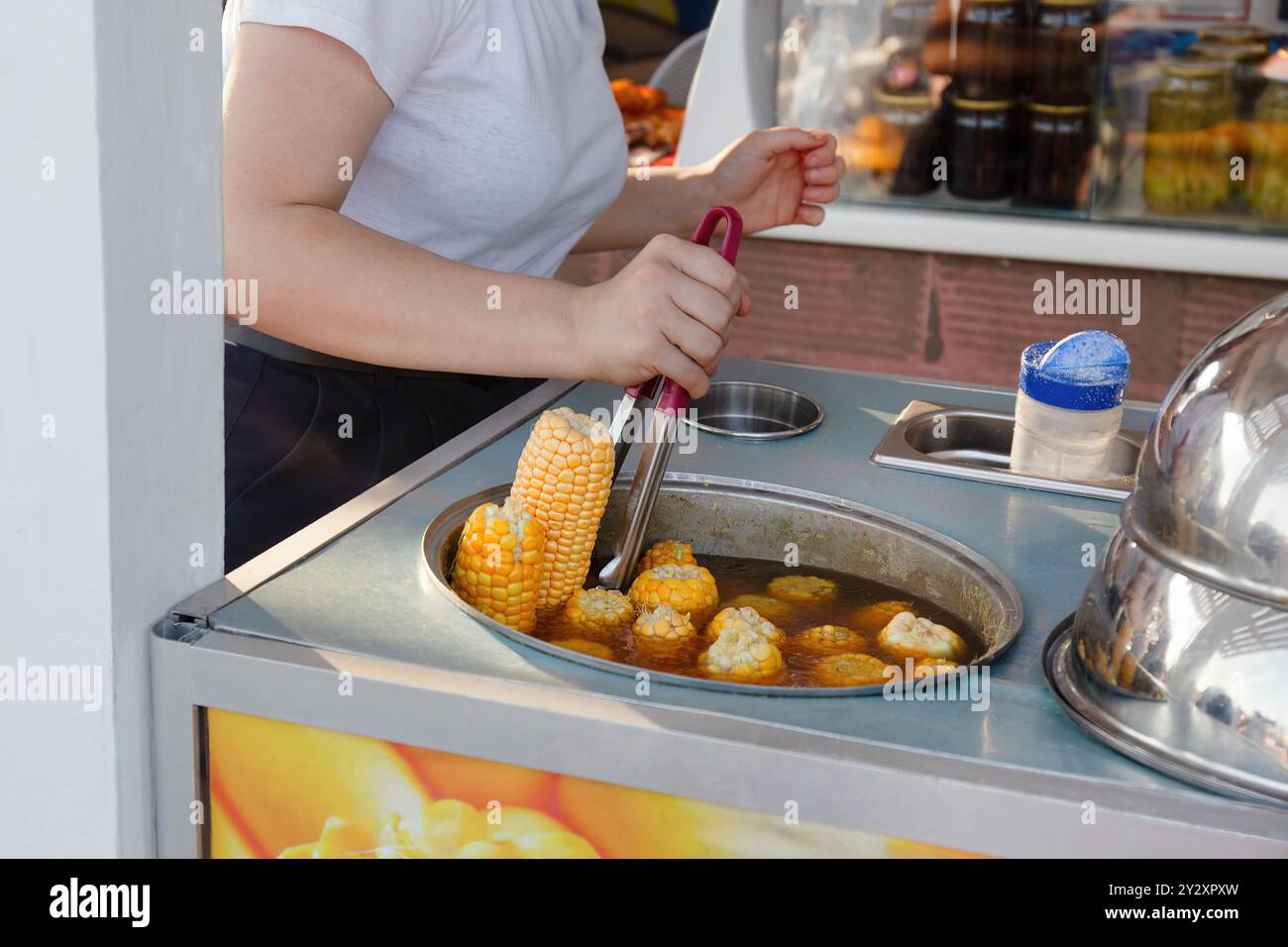 A market vendor uses tongs to grab hot corn cobs from boiling water ...