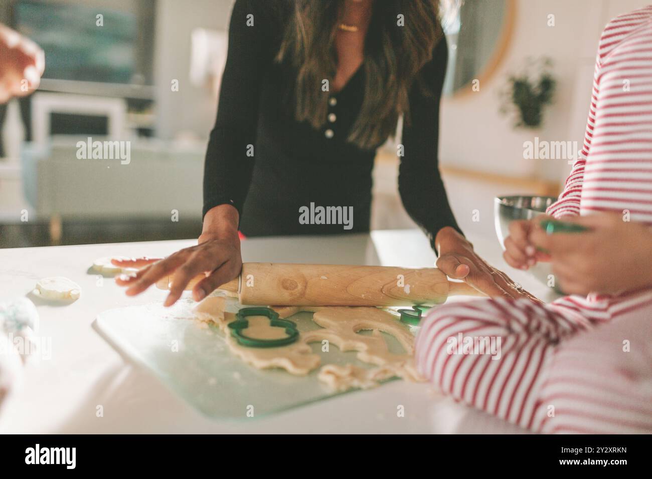 A woman rolling out cookie dough while making cookies with her children ...