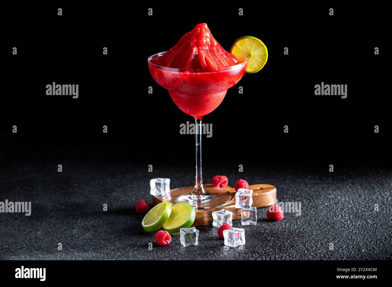 A raspberry frozen margarita garnished with a lime slice, surrounded by ...