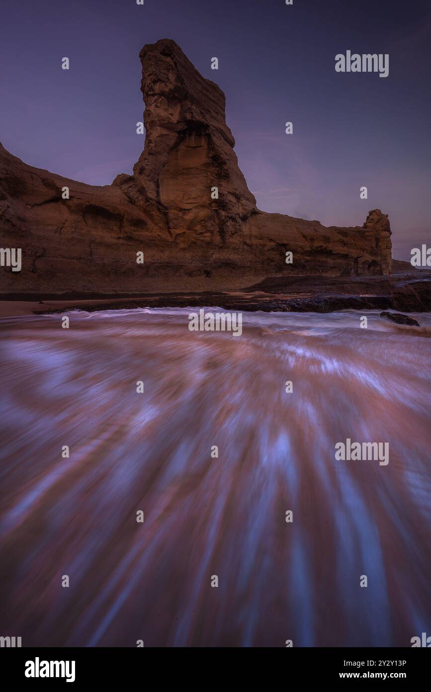 A stunning coastal rock formation at dusk with waves receding on the ...