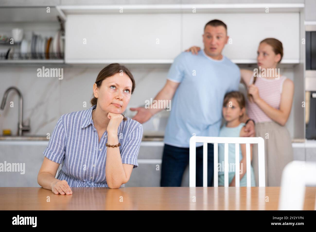 Sad mom is sitting near table in kitchen and listens to abuse of angry ...