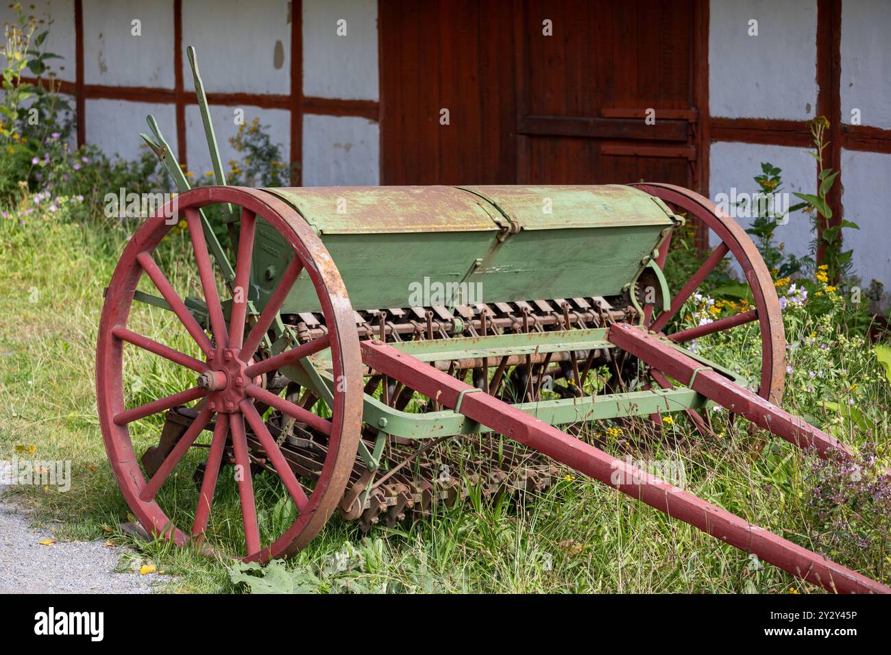 An old-fashioned green and red seed drill resting on grass, with a ...