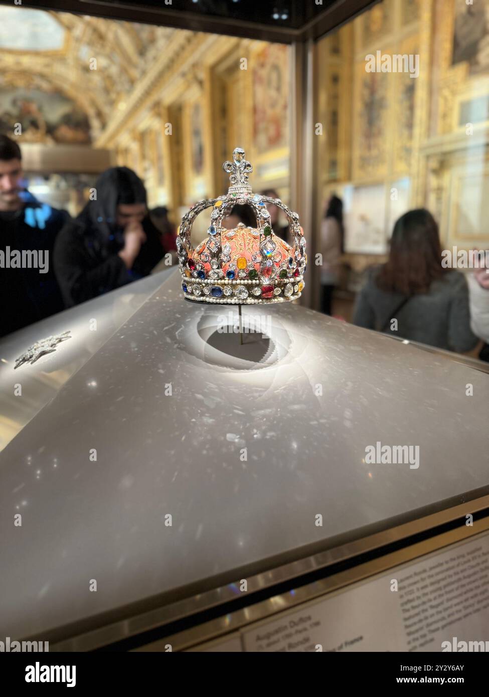 A detailed shot of a jeweled crown on display in a museum with people ...