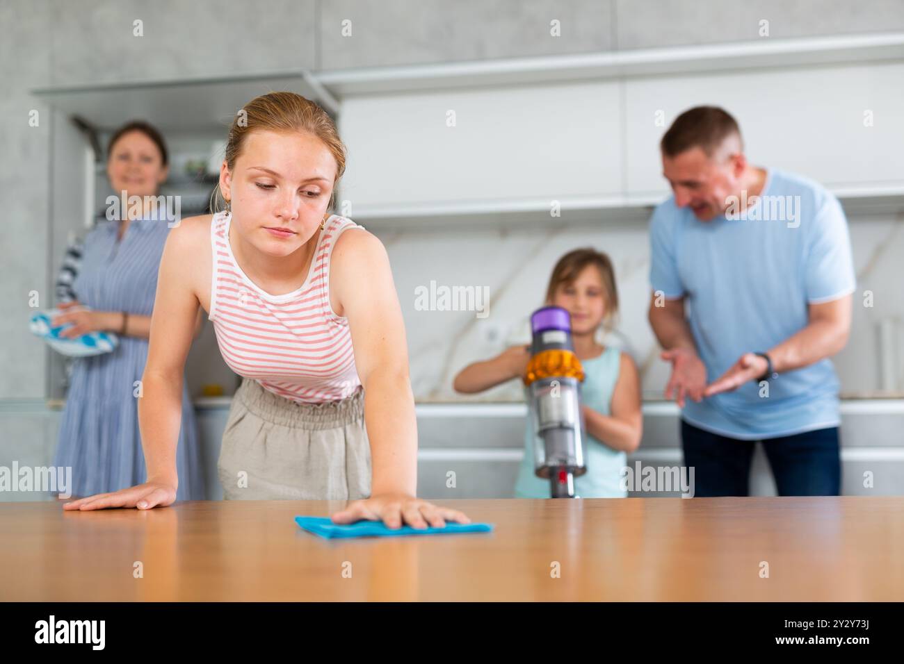 Teenage girl wiping kitchen table while cleaning apartment with family ...