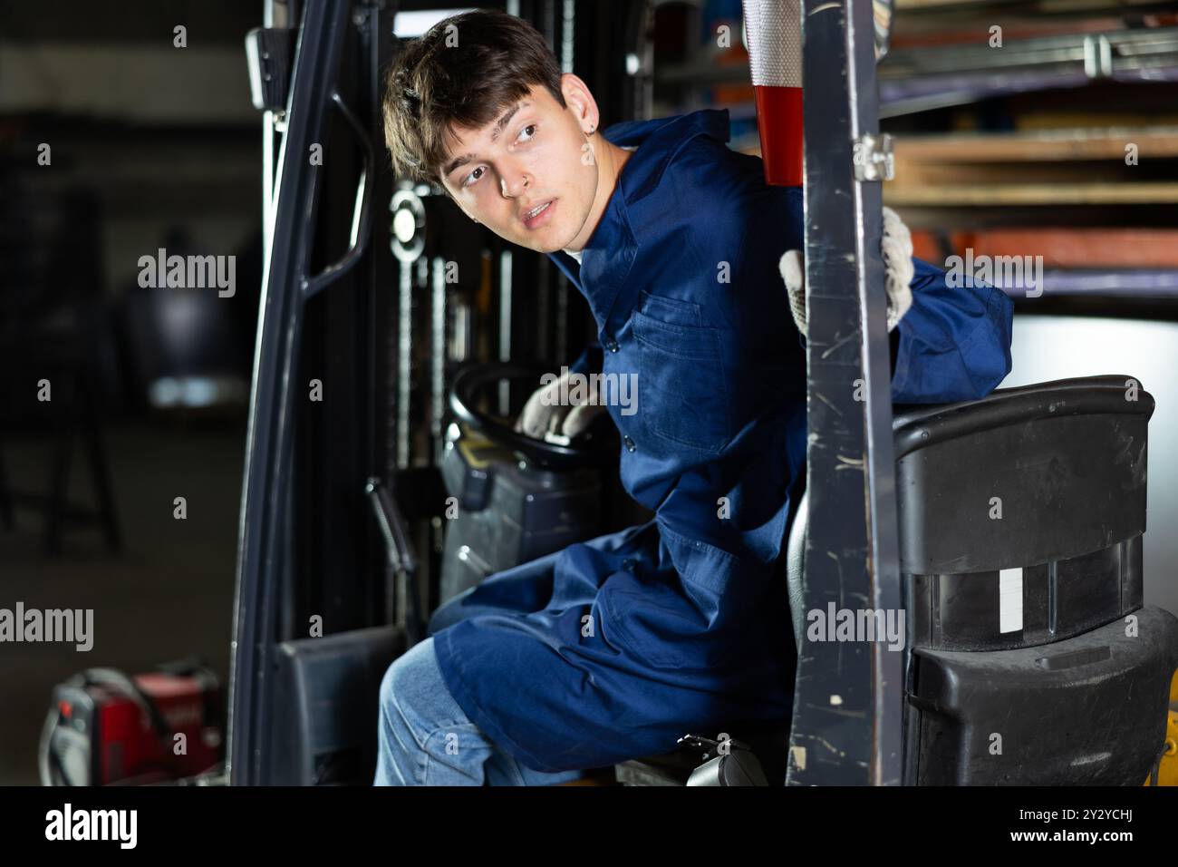 Young workman operating lift truck in industrial warehouse setting ...
