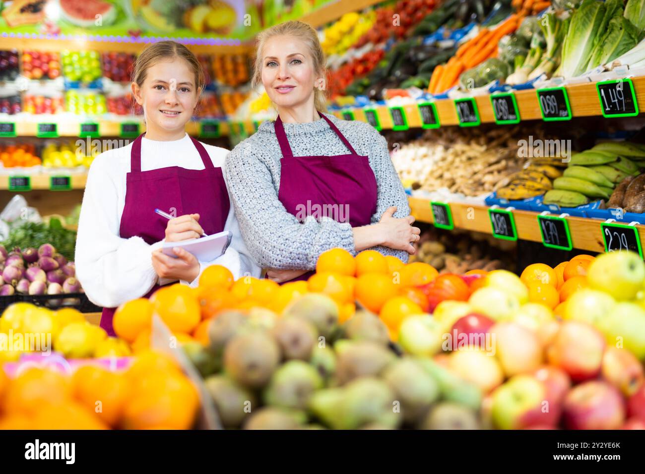 Confident female owner of greengrocery store posing with teen daughter ...