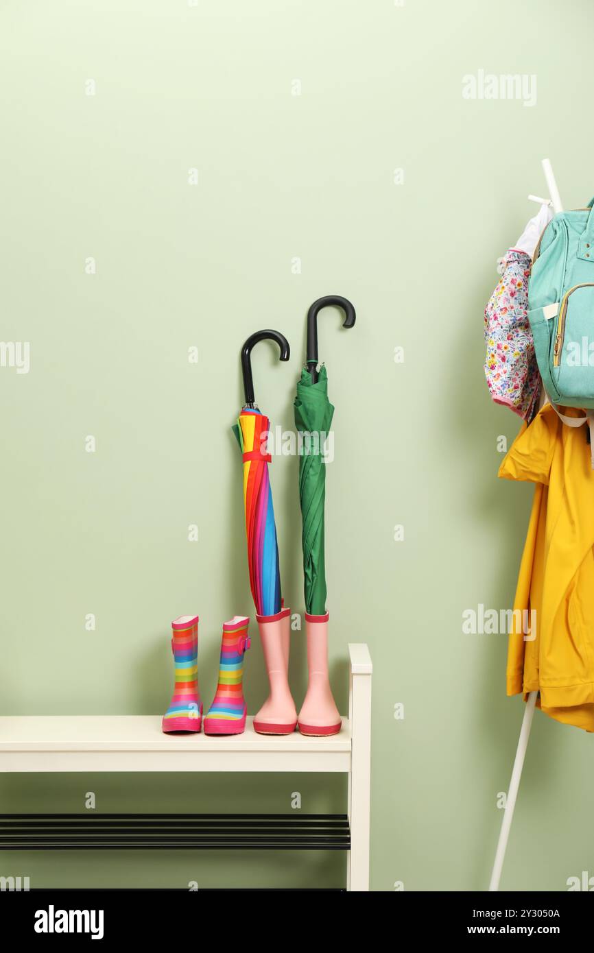 Colorful umbrellas, rubber boots and rack with jackets, backpack near green wall Stock Photo - Alamy