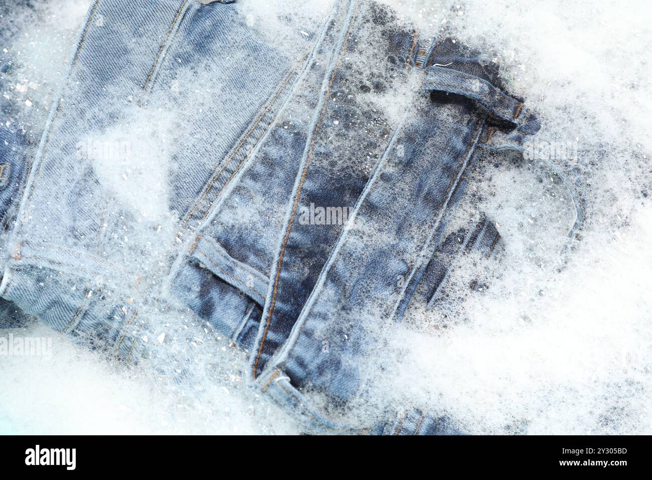 Many different denim clothes in basin with water and soap, top view ...