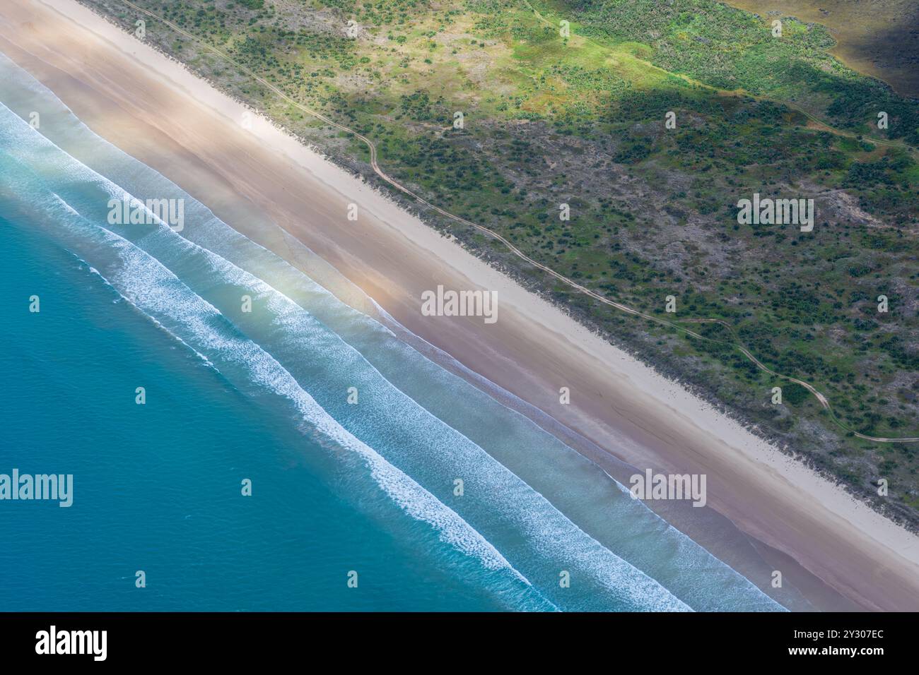 An aerial view of a long stretch of sandy beach flanked by green ...