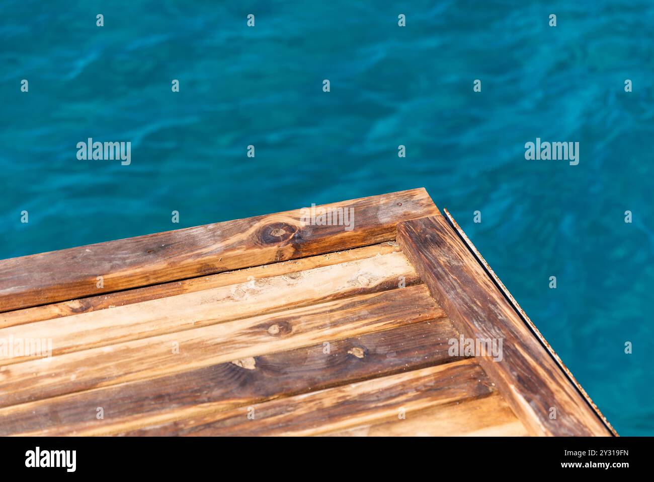 Corner of an empty wooden pier is on the blurred blue sea water ...