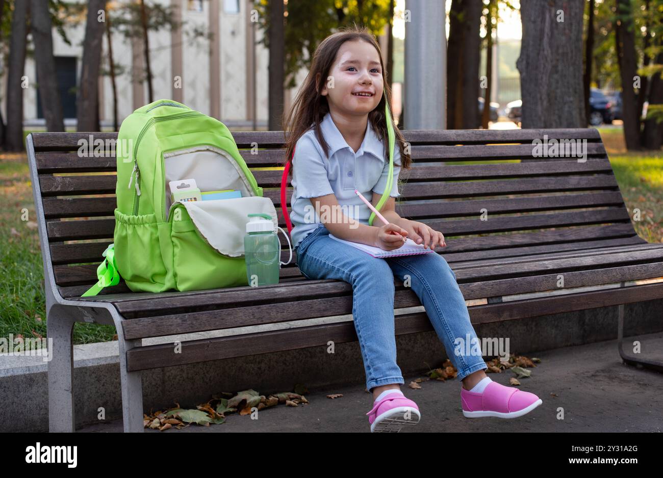 Happy young girl with backpack sitting on park bench, writing in ...