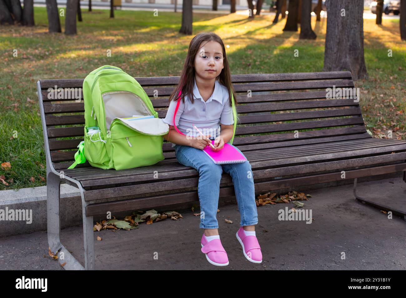 Young girl with backpack sitting on bench writing in notebook outdoors ...