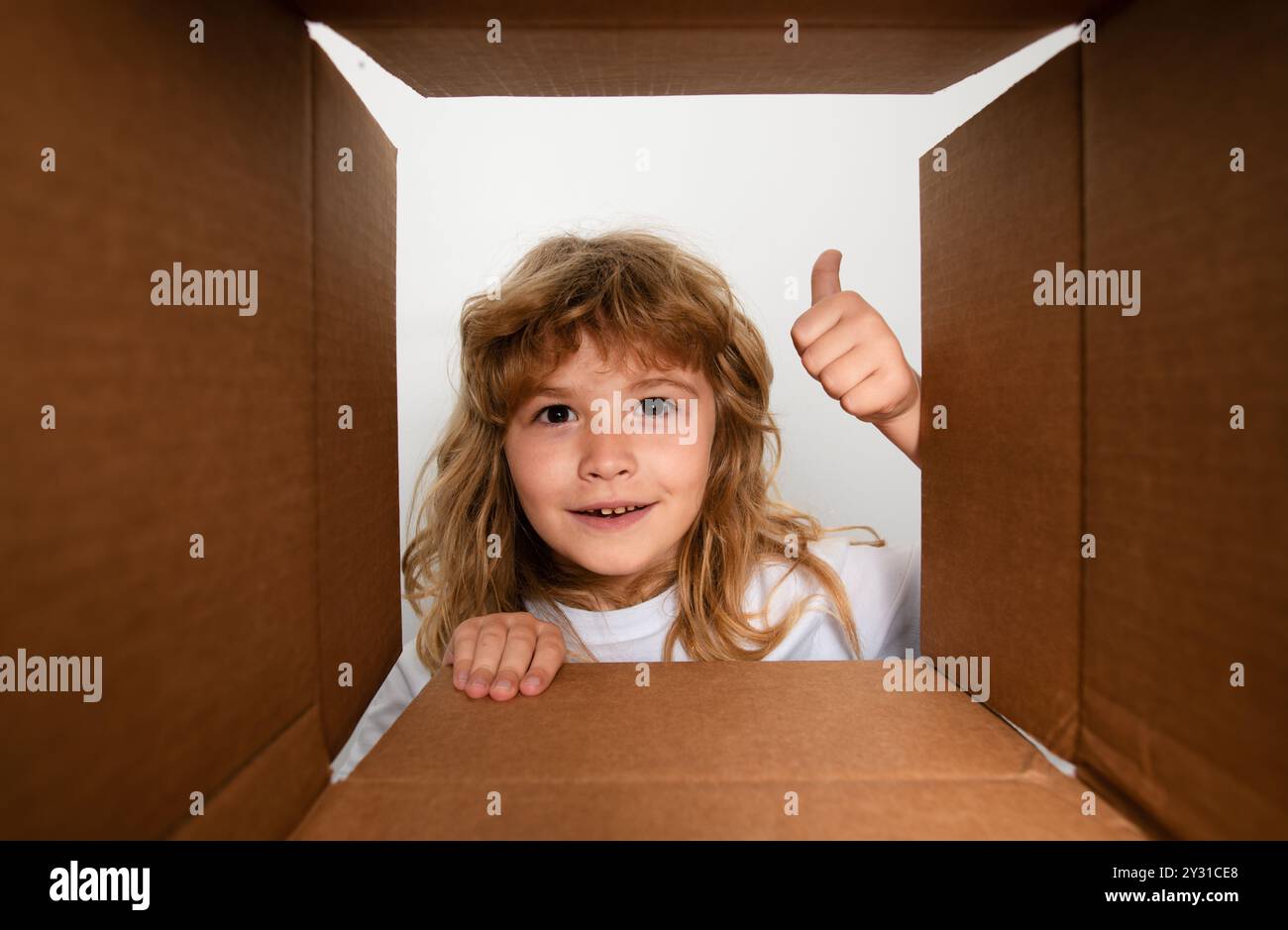 Funny child boy with thumb up is opening gift and looking inside ...