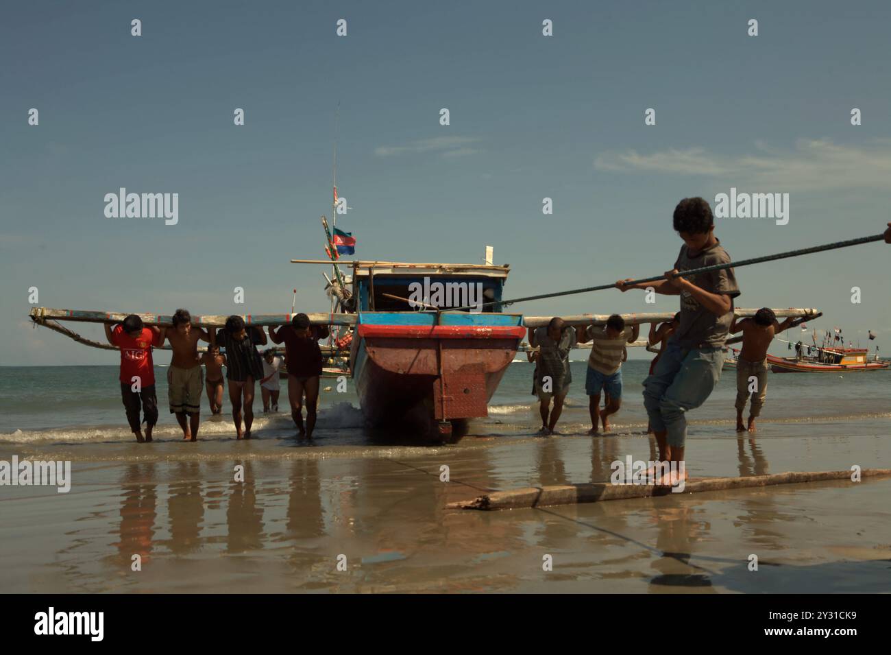 Men pushing and pulling a fishing boat with a rope on Malabero beach, a ...