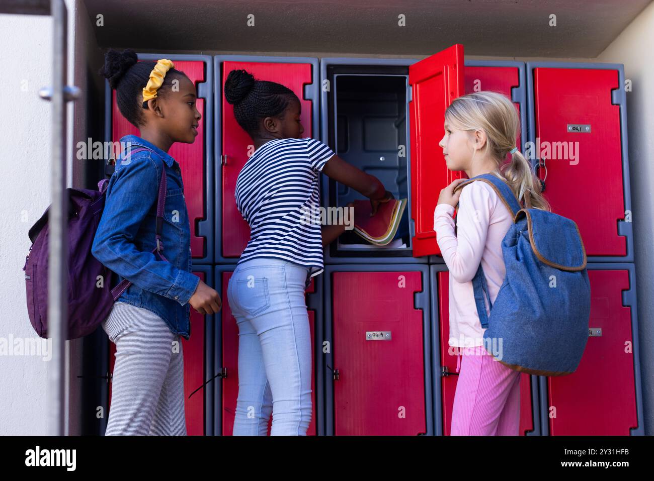At school, opening lockers, three multiracial girls organizing books ...