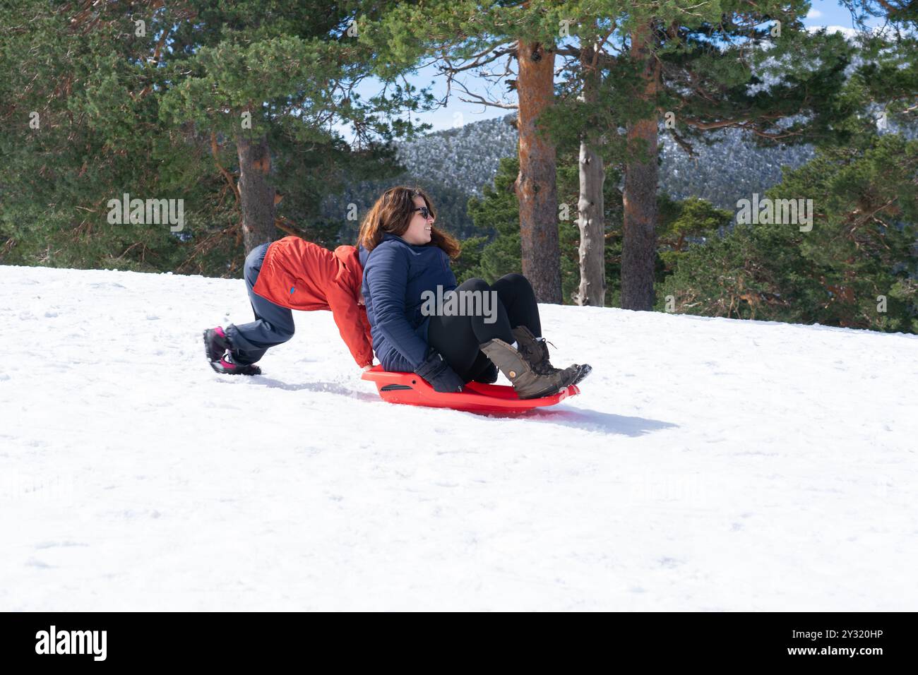 Boy pushing his mother on a sled in the snow Stock Photo - Alamy