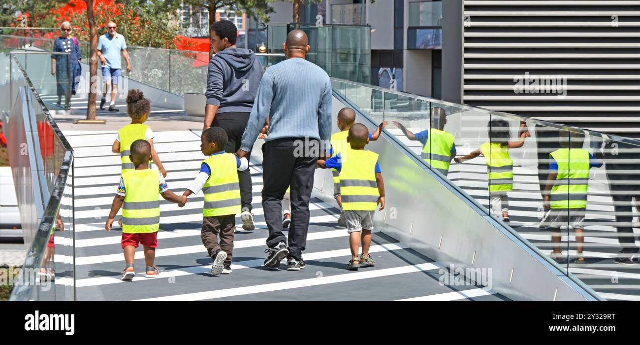 Back view two adult carers walking elevated public pavement five young ...