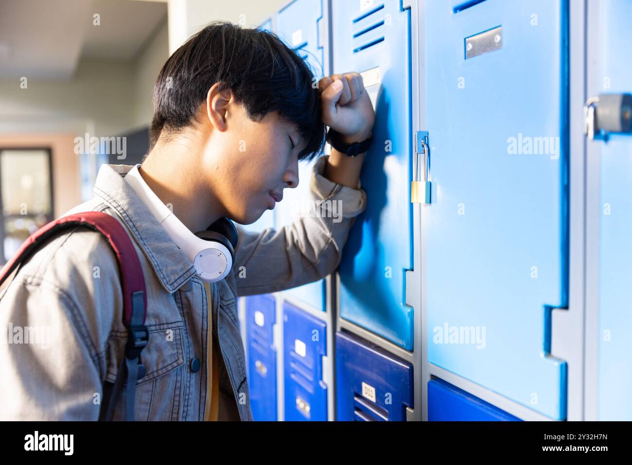 Leaning against locker, stressed asian teenage boy in school hallway ...