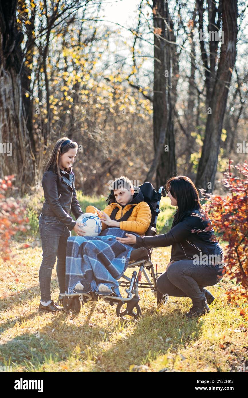 Mother and sibling engaging child in wheelchair in outdoor play with ...