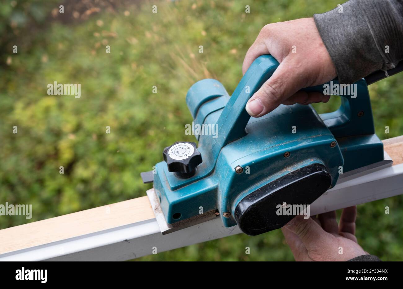 Carpenter planes a wooden window outdoors with an electric planer ...