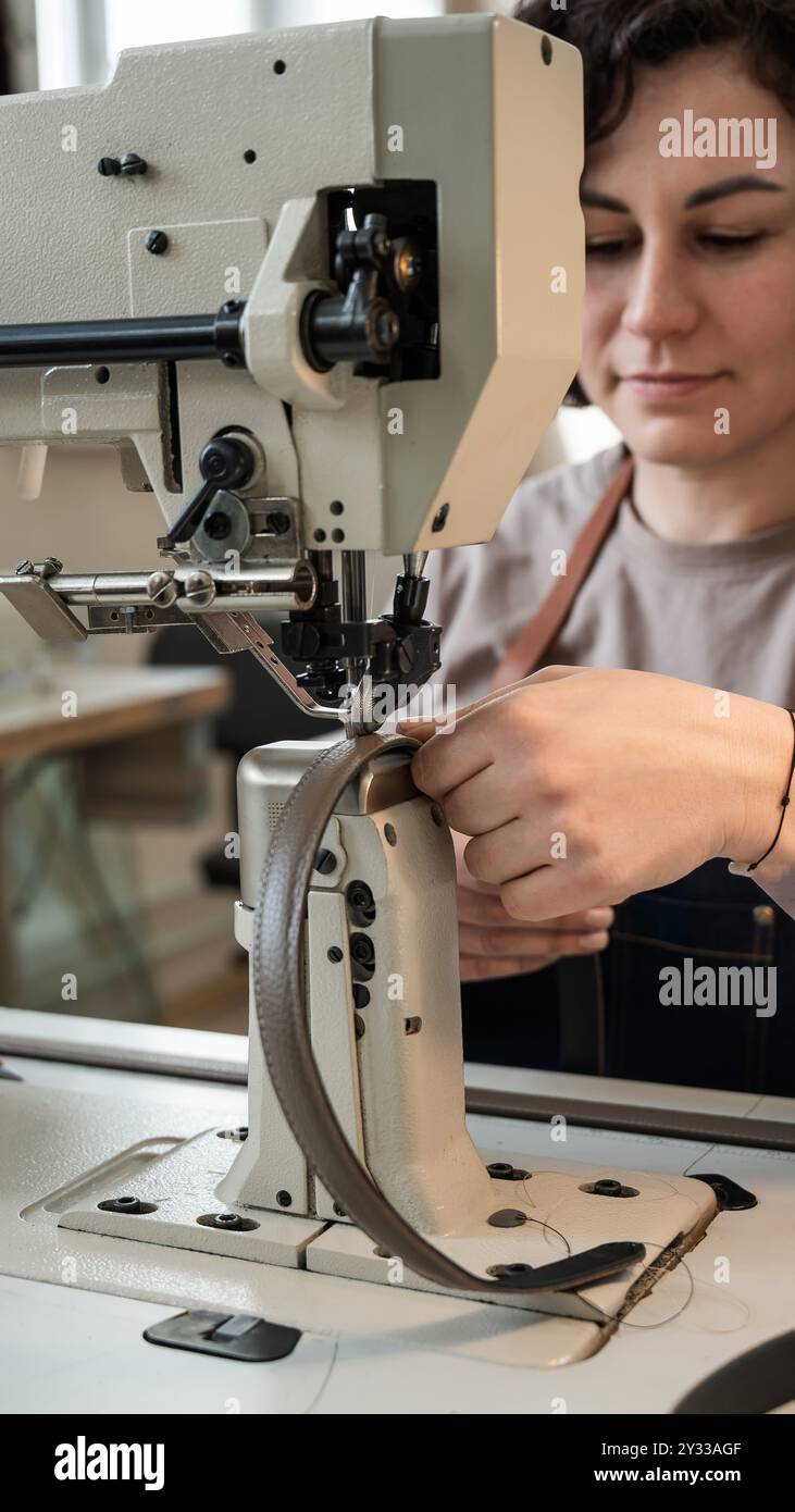 A woman tanner sews a leather belt on a sewing machine. Vertical photo ...