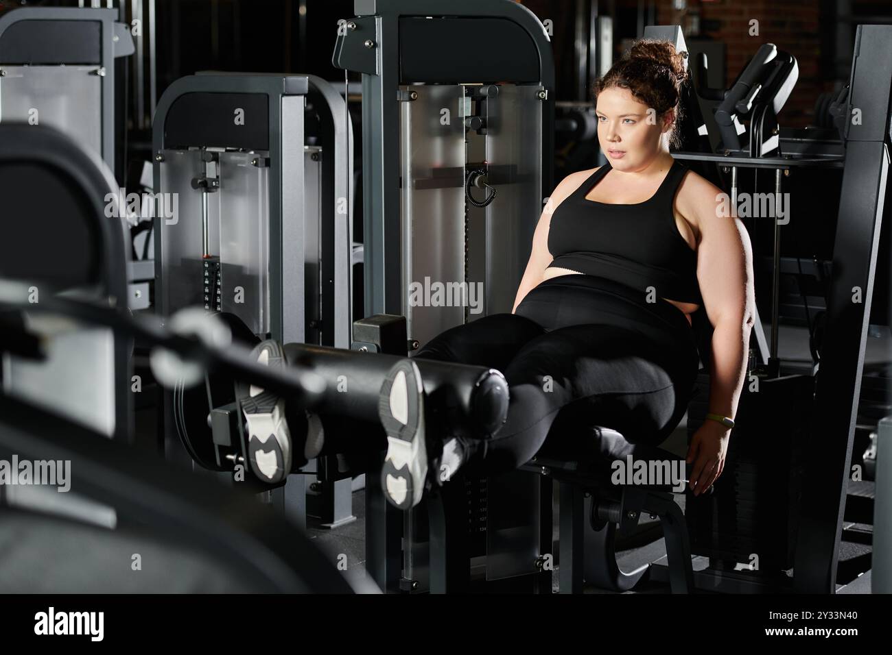 A plus-size woman focuses intently while working out on gym equipment ...