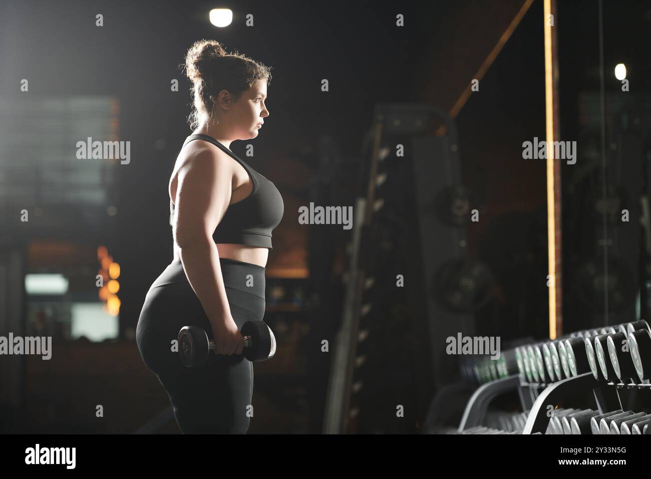 A young plus-size woman confidently lifts weights, promoting strength ...
