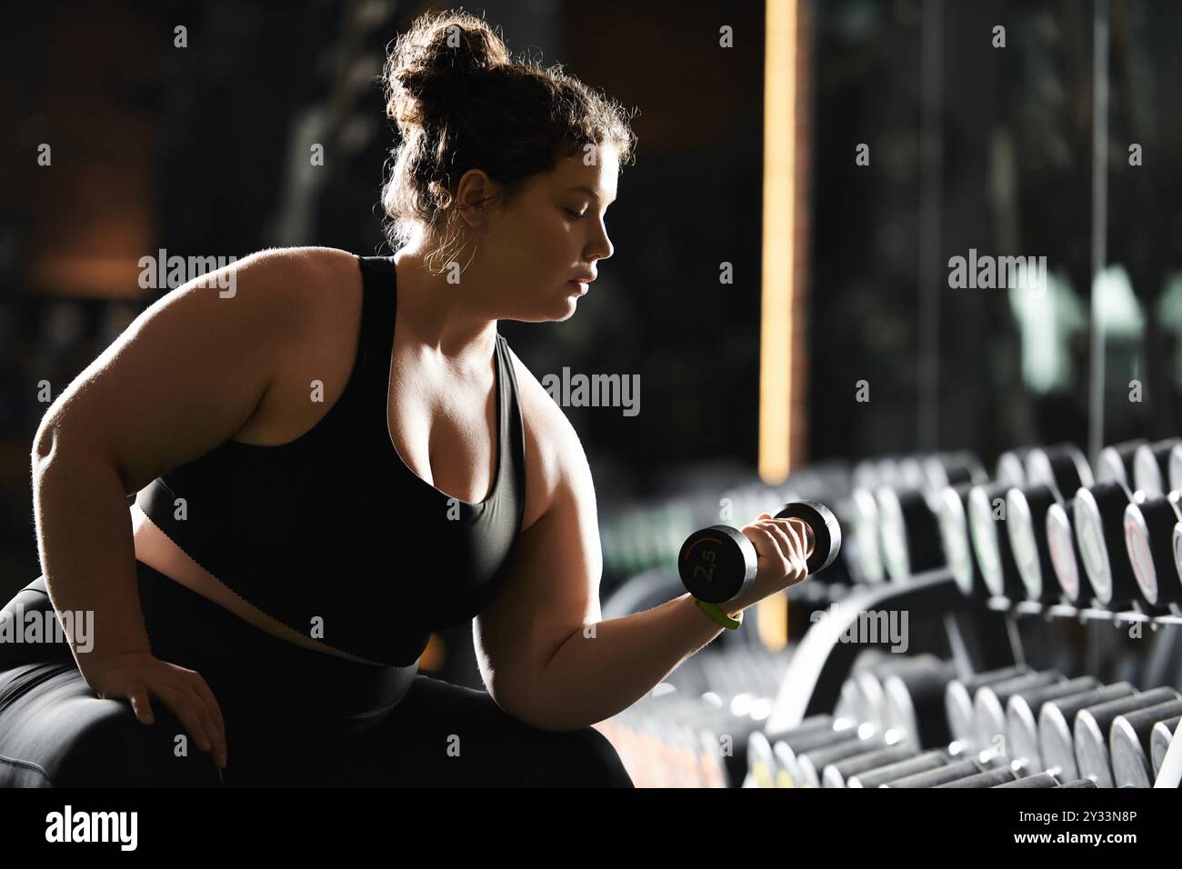 A young plus-size woman focuses on her workout, lifting a dumbbell with ...