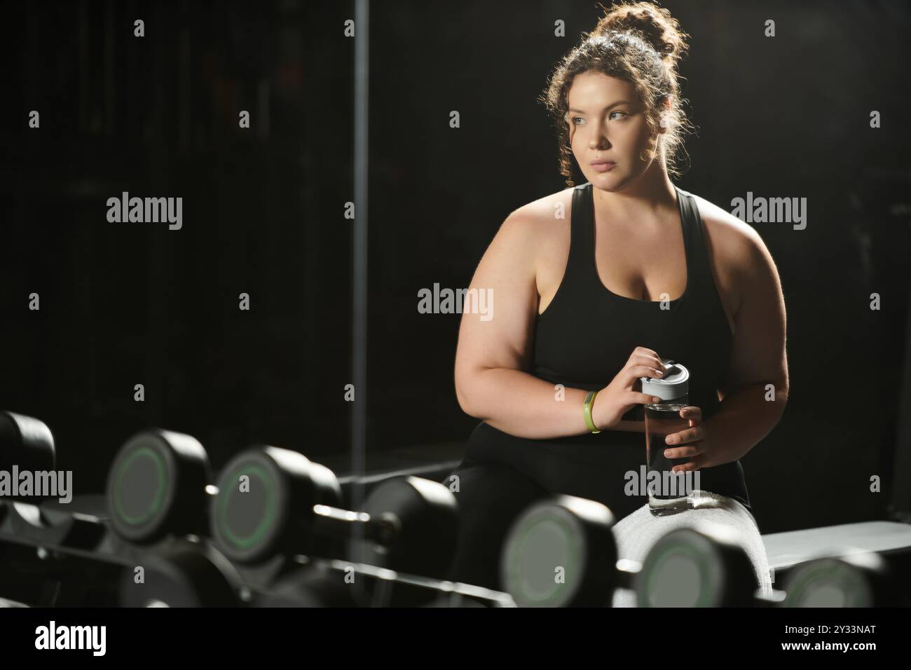 A plus-size woman lifts a water bottle, focused on her workout in a ...