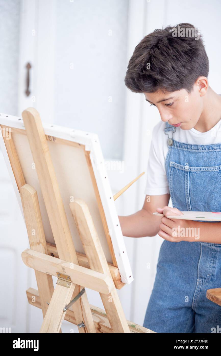 A boy is painting a picture on a canvas. He is completely concentrated ...