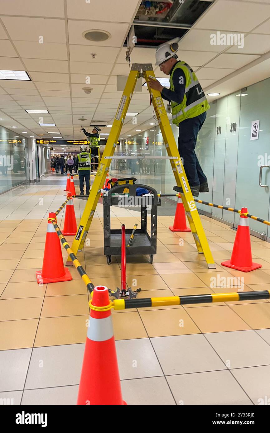 A man in a yellow safety vest is on a ladder in a building. There are ...