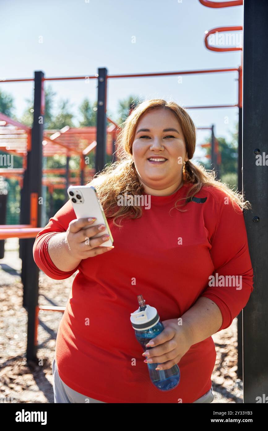 A happy plus size woman exercising outdoors, holding her phone and ...