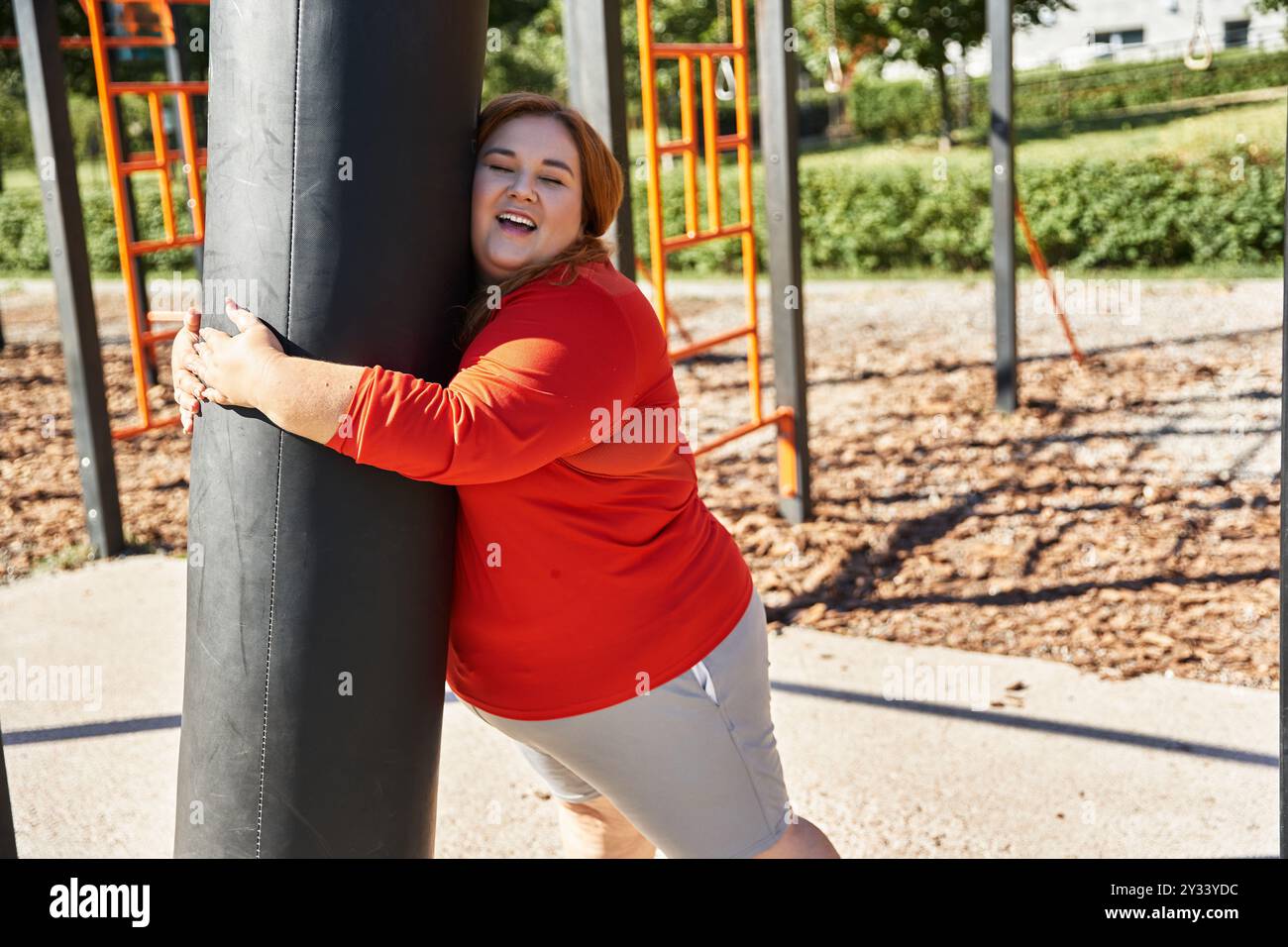A plus size woman embraces a fitness pole while exercising outdoors ...