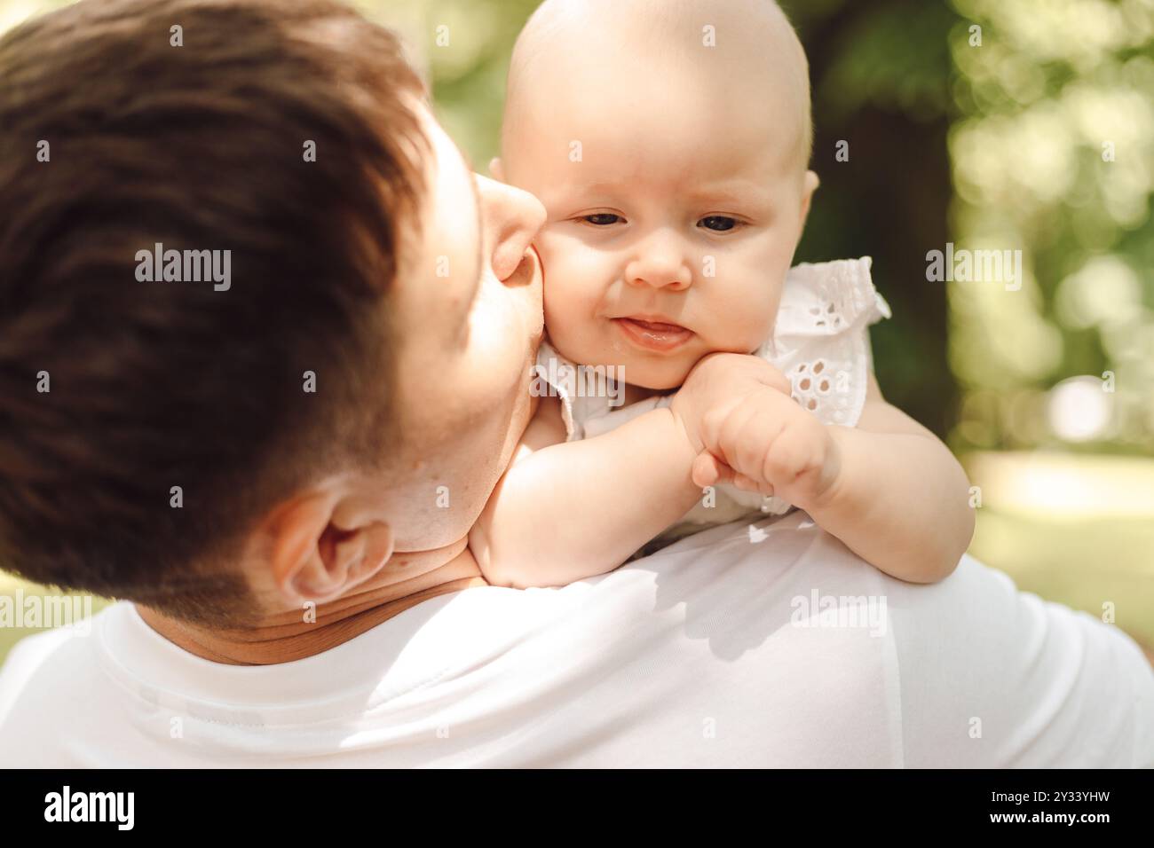 A man with a happy gesture is holding a baby in his arms, kissing its ...
