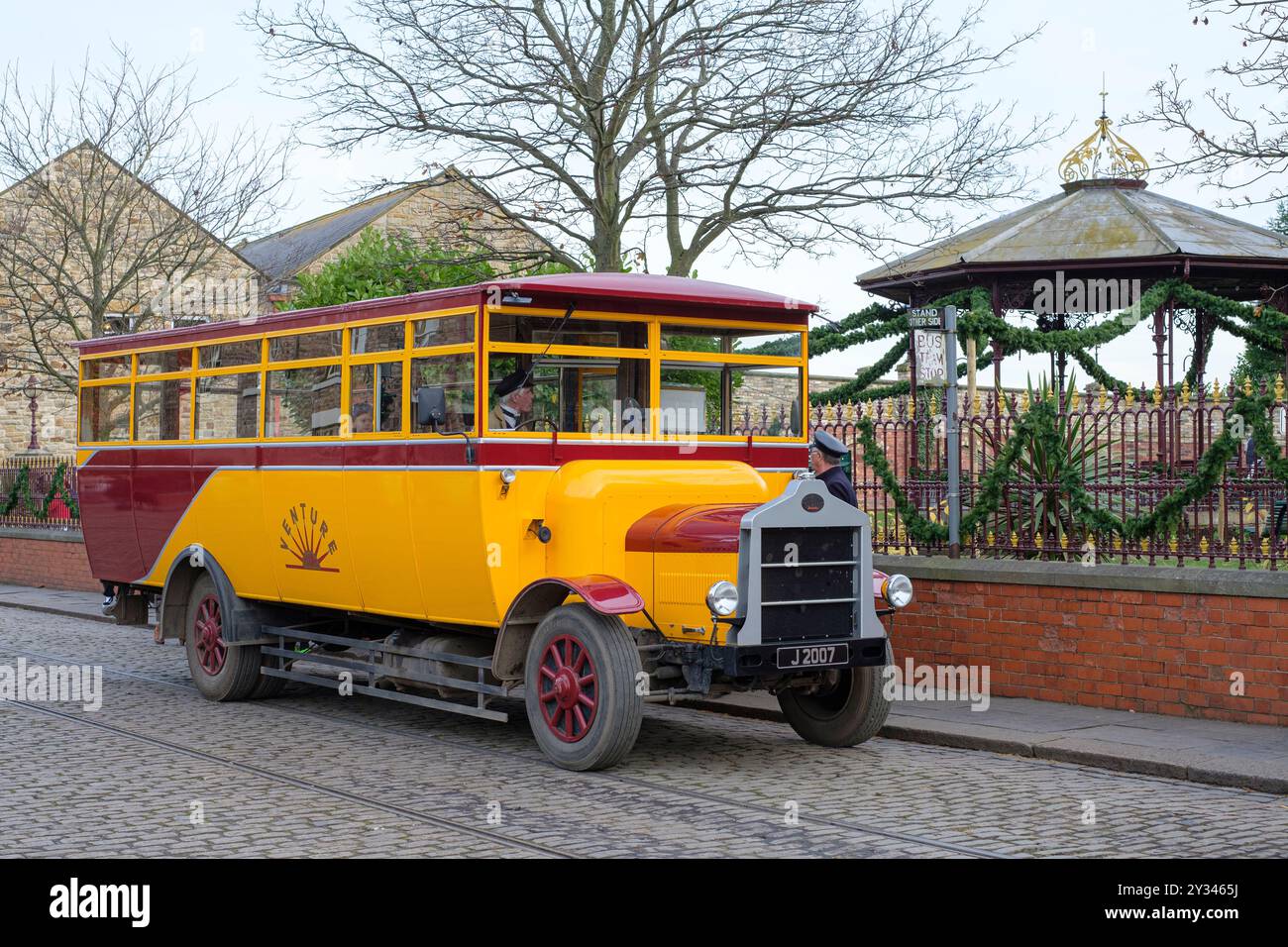 An old yellow and maroon bus parked at the pavement with driver waiting ...