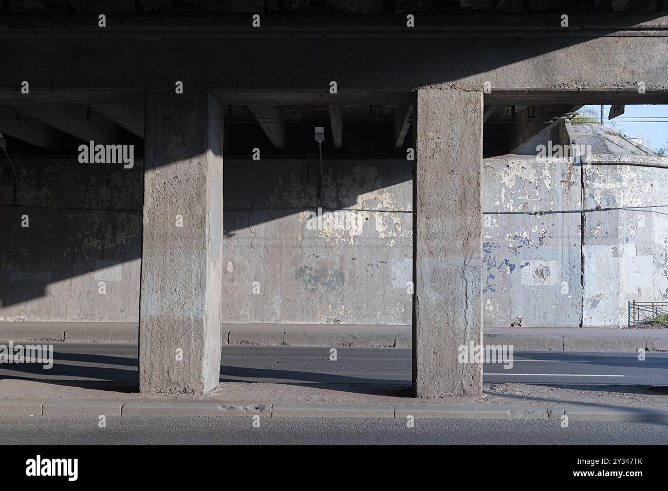 Concrete pillars supporting a bridge, casting shadows on a street ...