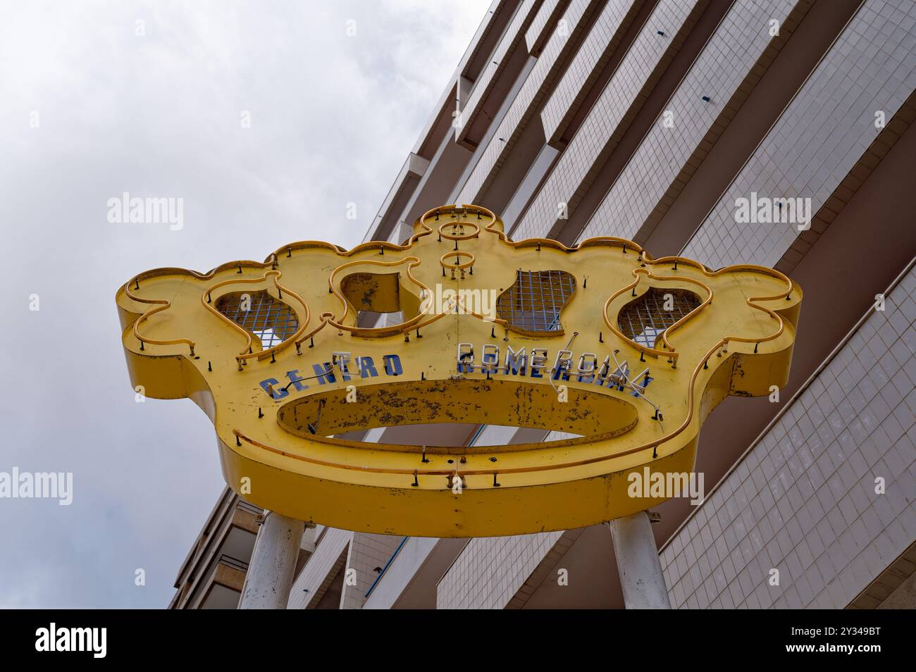 A weathered yellow sign shaped like a crown stands tall, reading ...