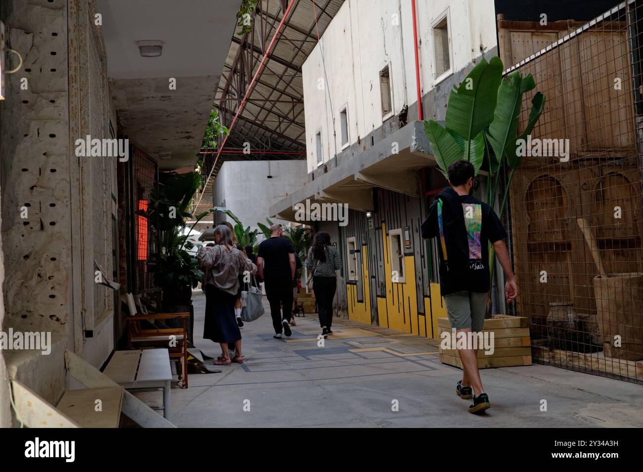 People walk through a vibrant, plant-filled alley in an industrial ...