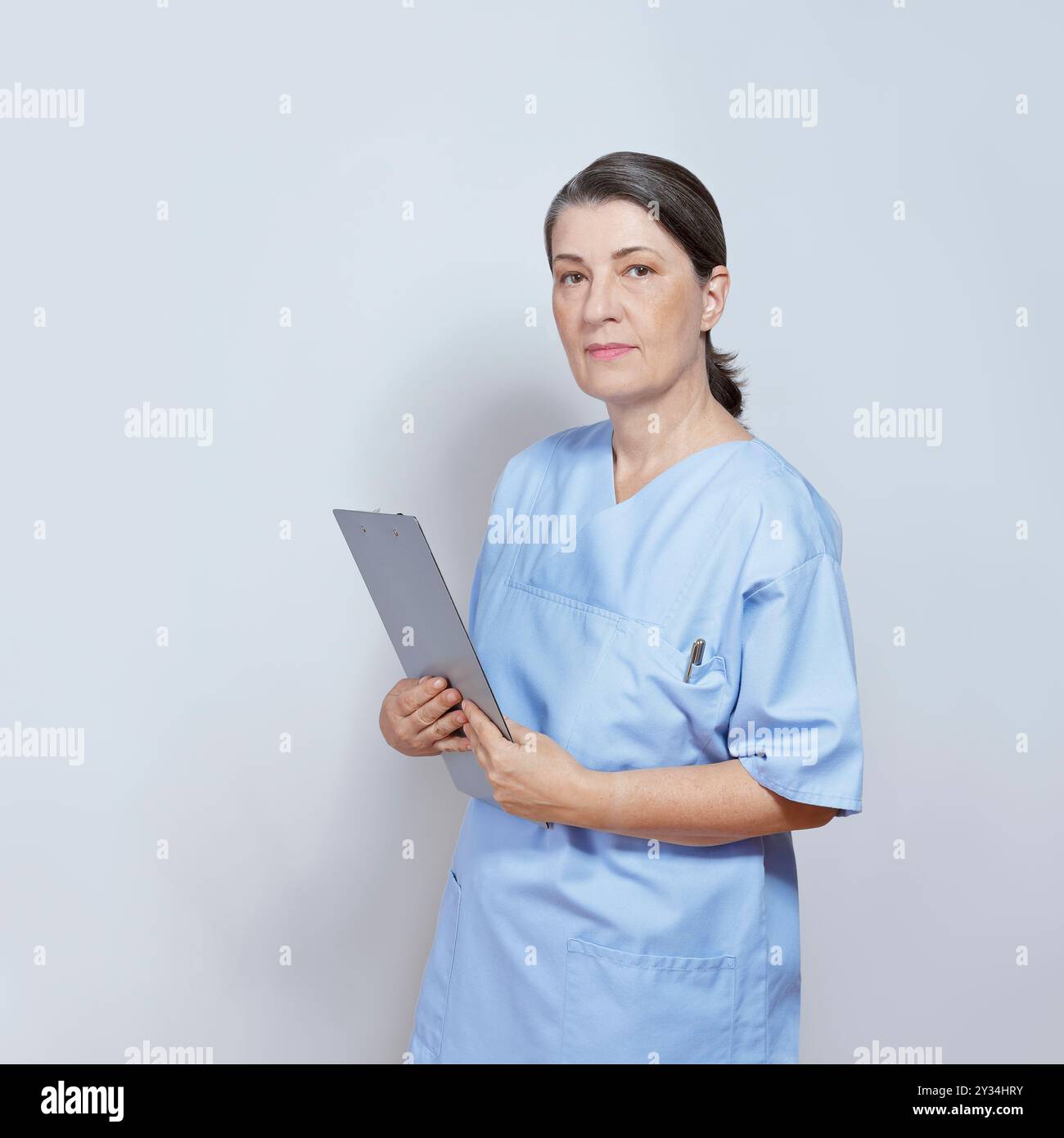 Portrait of a stern looking middle aged nurse in a blue scrub holding a ...