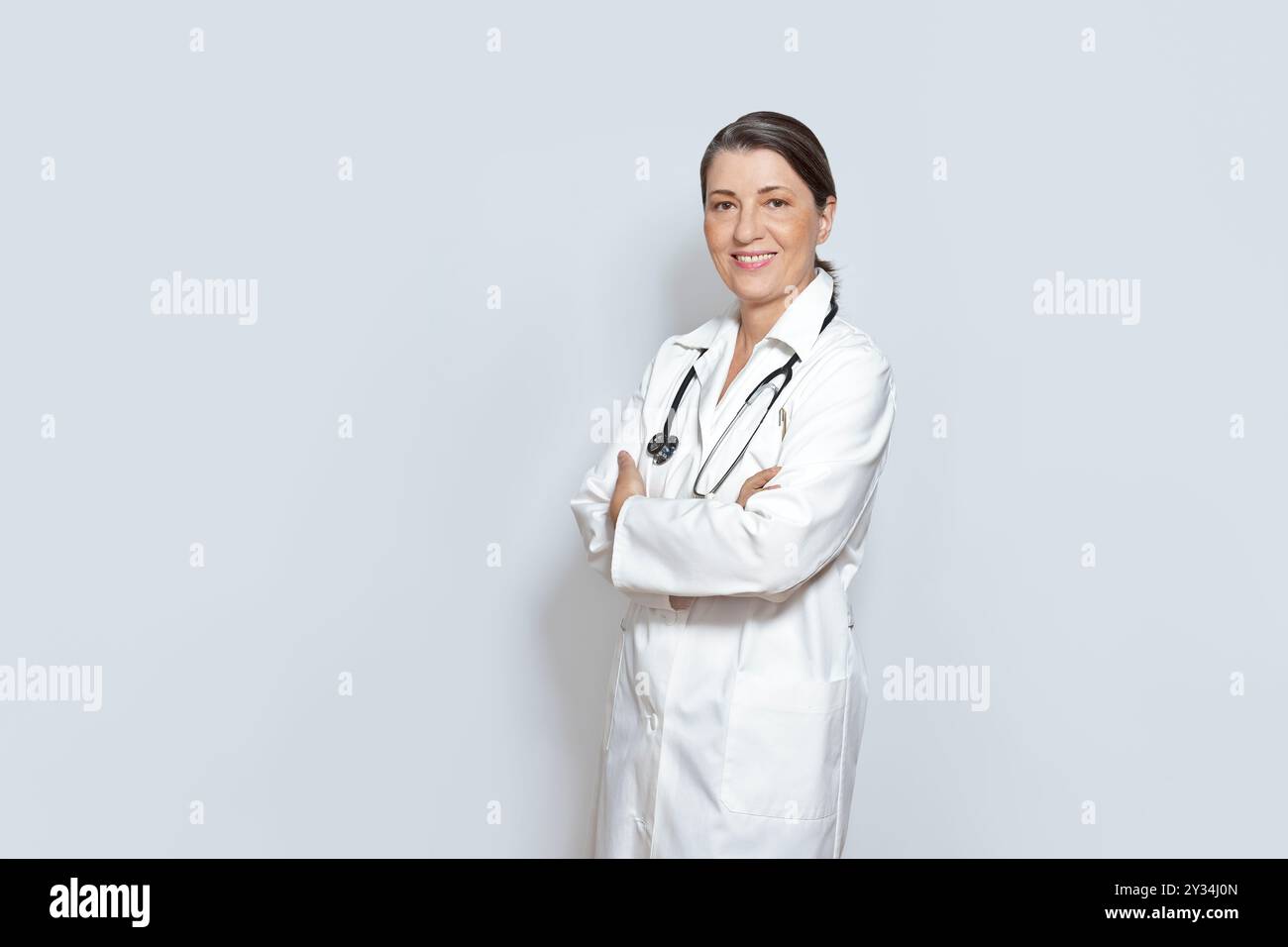 Older female doctor in a white lab coat, smiling friendly, on neutral ...