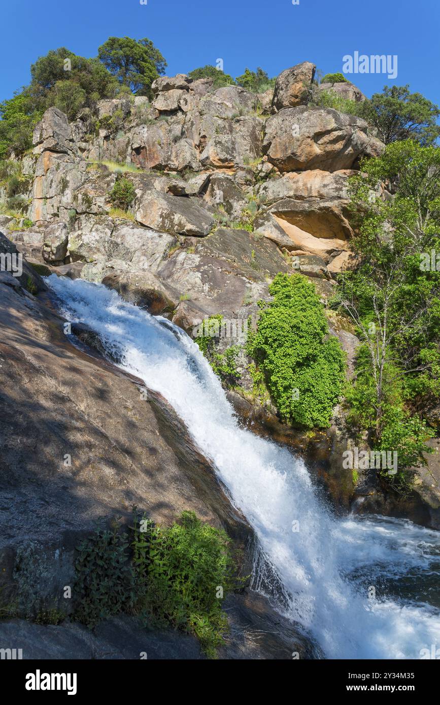 A mighty waterfall flows over large rocks in a forest landscape under a ...