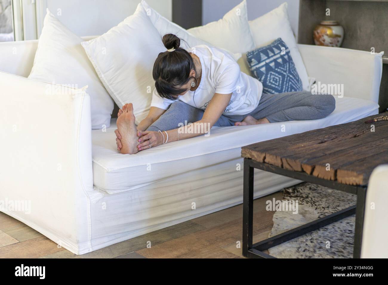 Mid-adult woman practicing stretching exercises on her sofa, enjoying ...