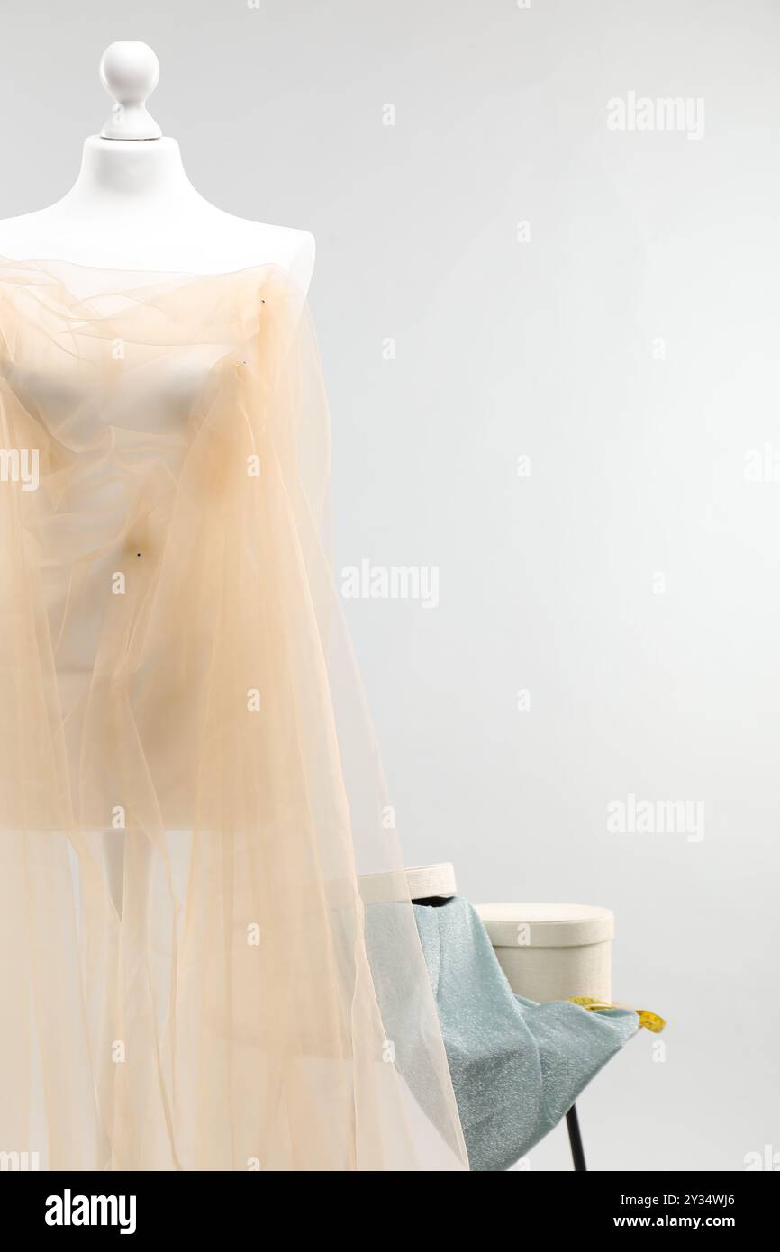 Mannequin with fabric and boxes on side table against light grey ...