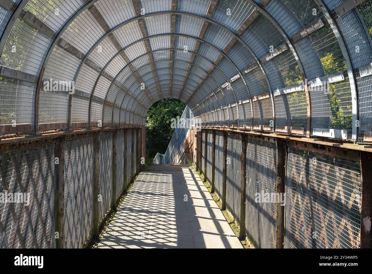 Metal cage-like enclosed arched tunnel footbridge over a railway line ...