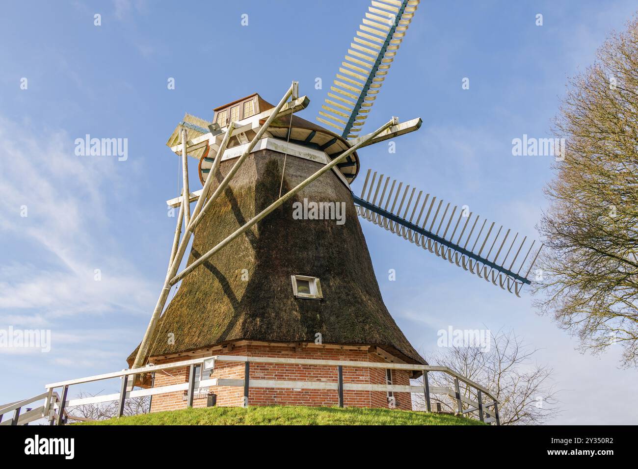 Windmill with thatched roof and large wooden poles in front of a clear ...